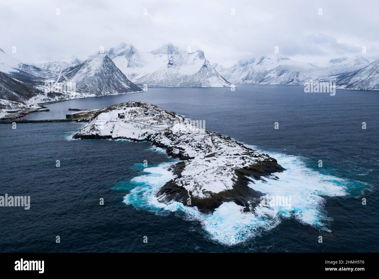 Aerial view of Husoy Island with strong surf in front of mountain range ...