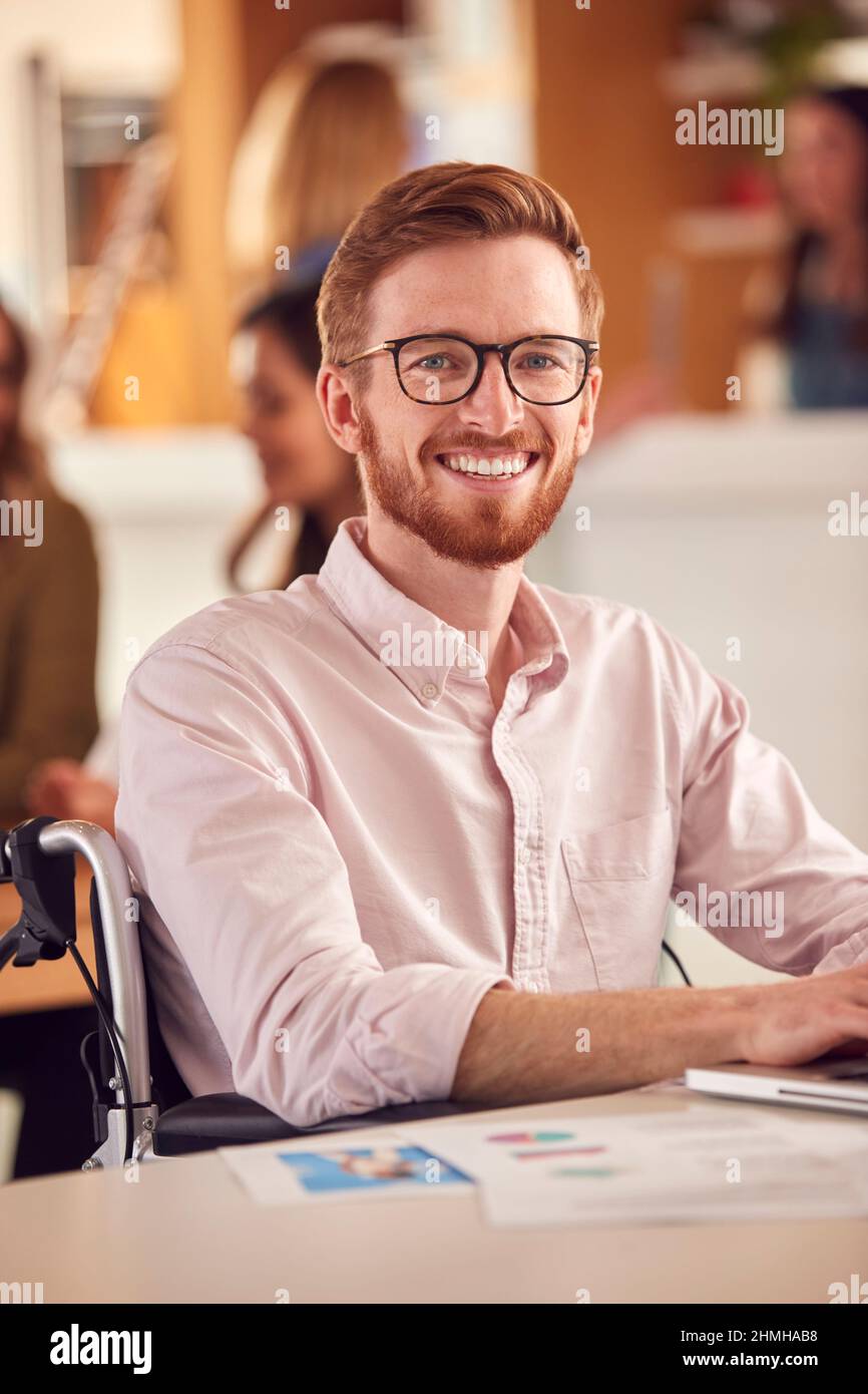 Portrait Of Businessman In Wheelchair Sitting At Desk Working On Laptop ...