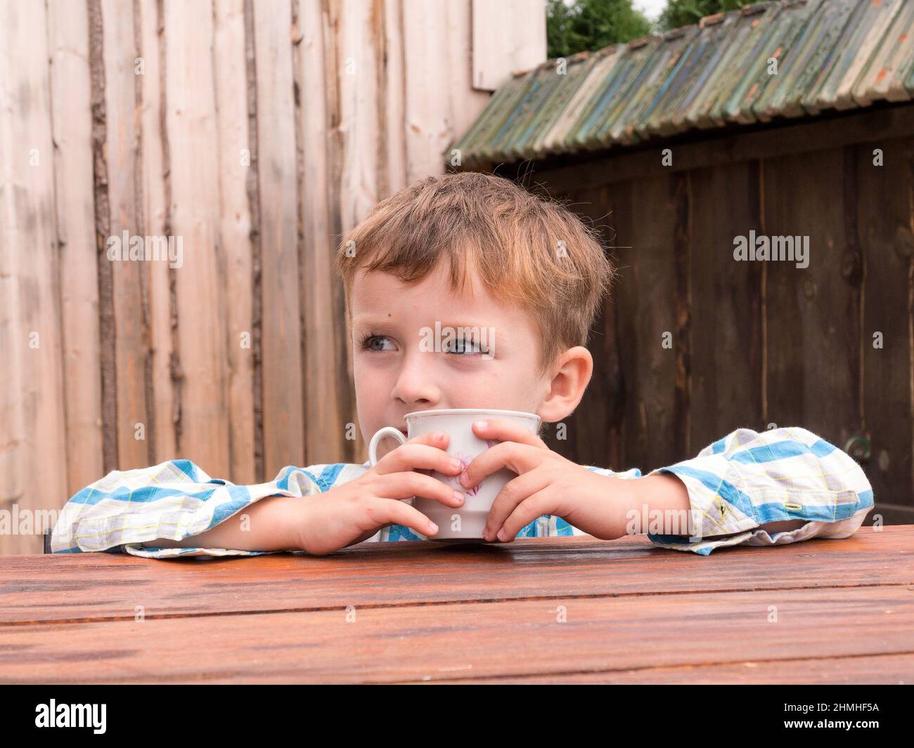 Boy is sitting at wooden table with cup of tea and looking into ...
