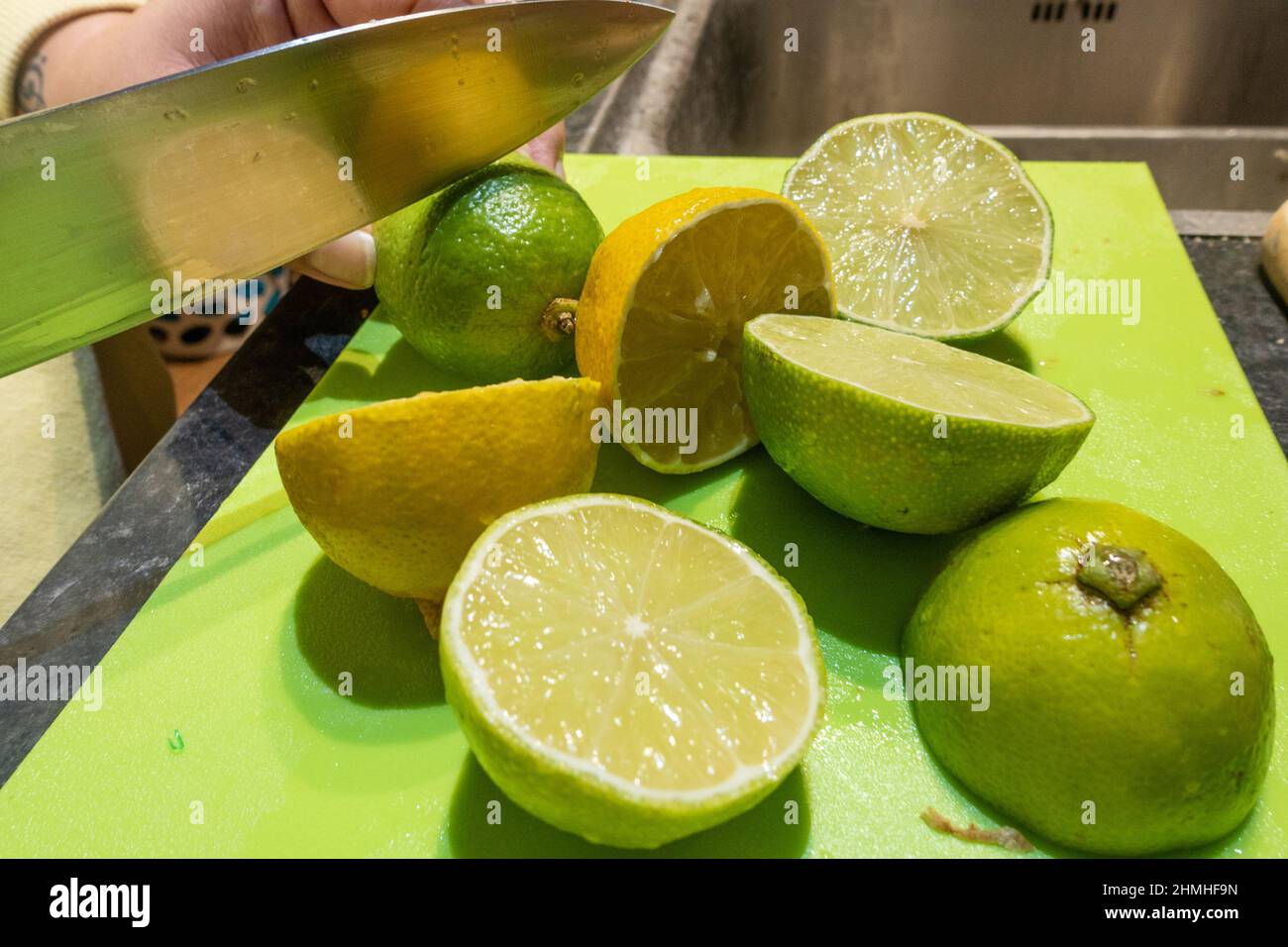 Slicing lemons and limes with a kitchen knife on a green chopping board ...