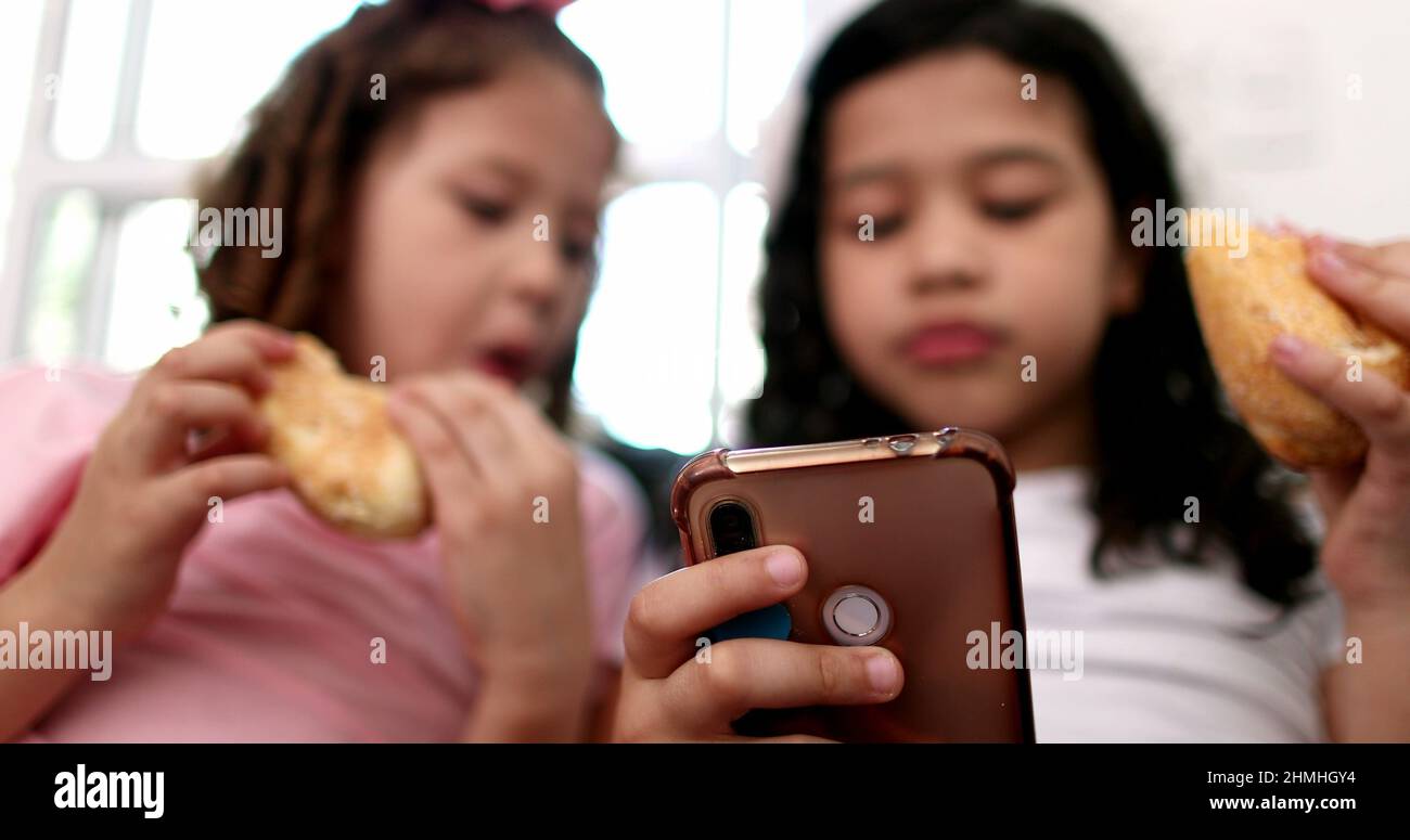 Generation Z little girls using mobile phone while eating sandwich ...