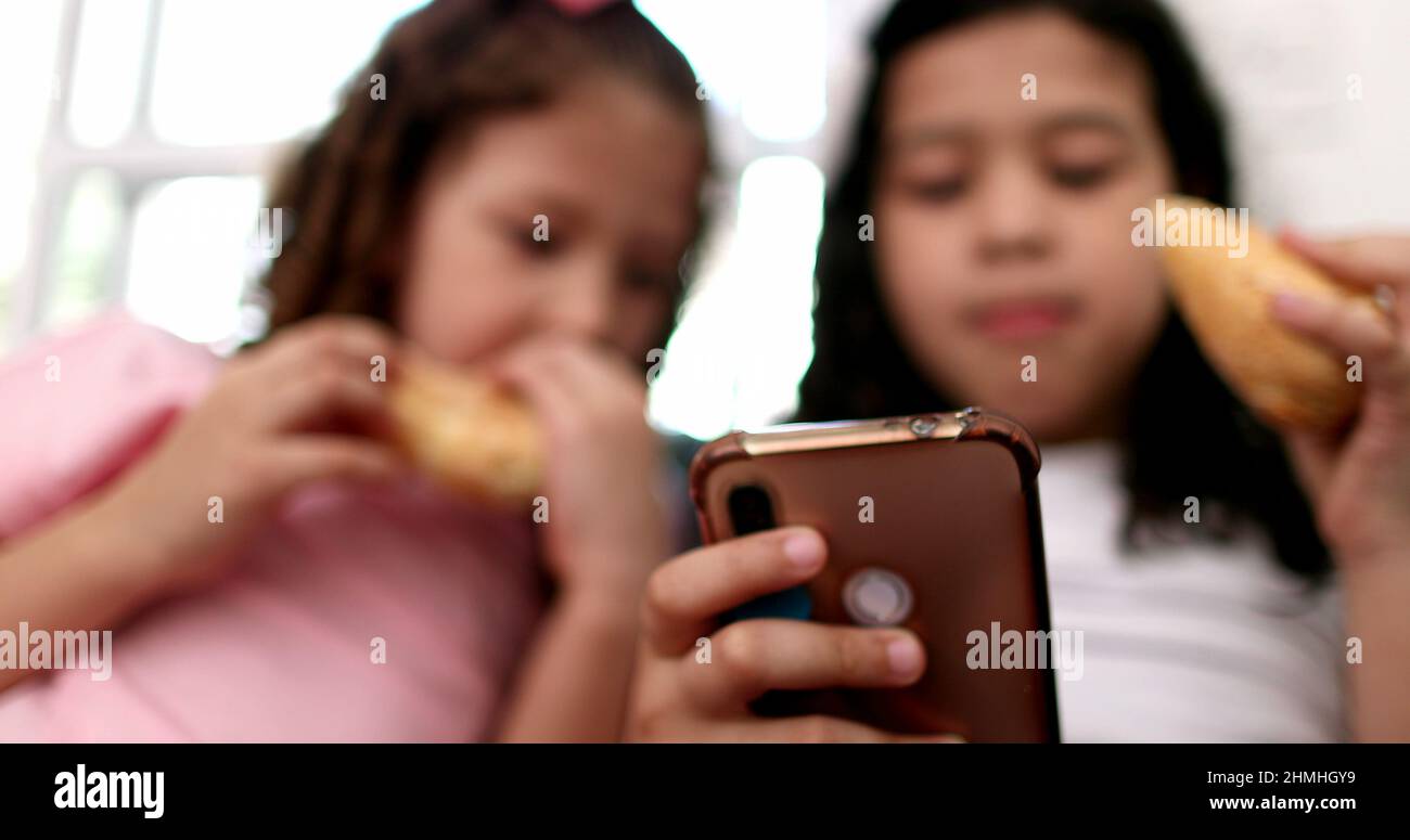 Generation Z little girls using mobile phone while eating sandwich ...