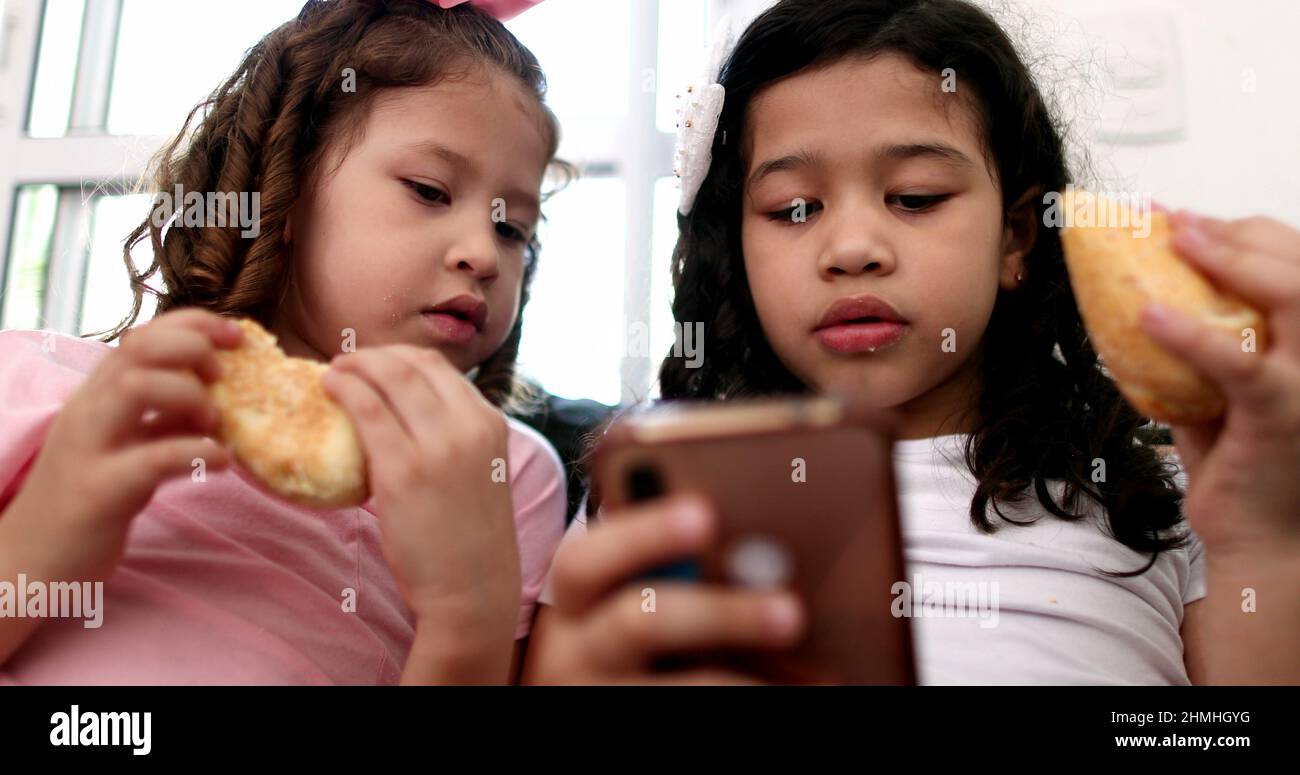 Generation Z little girls using mobile phone while eating sandwich ...