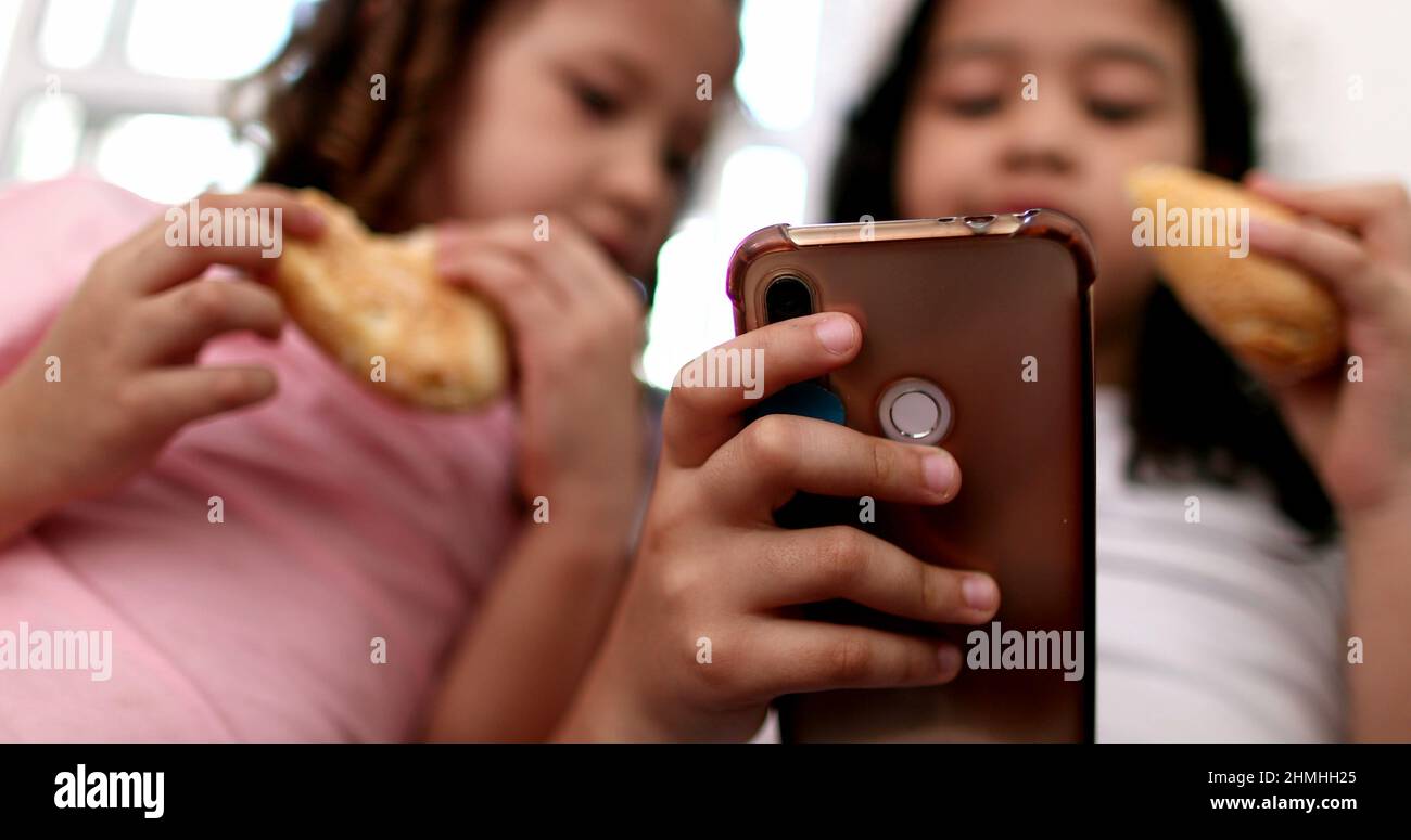 Generation Z little girls using mobile phone while eating sandwich ...