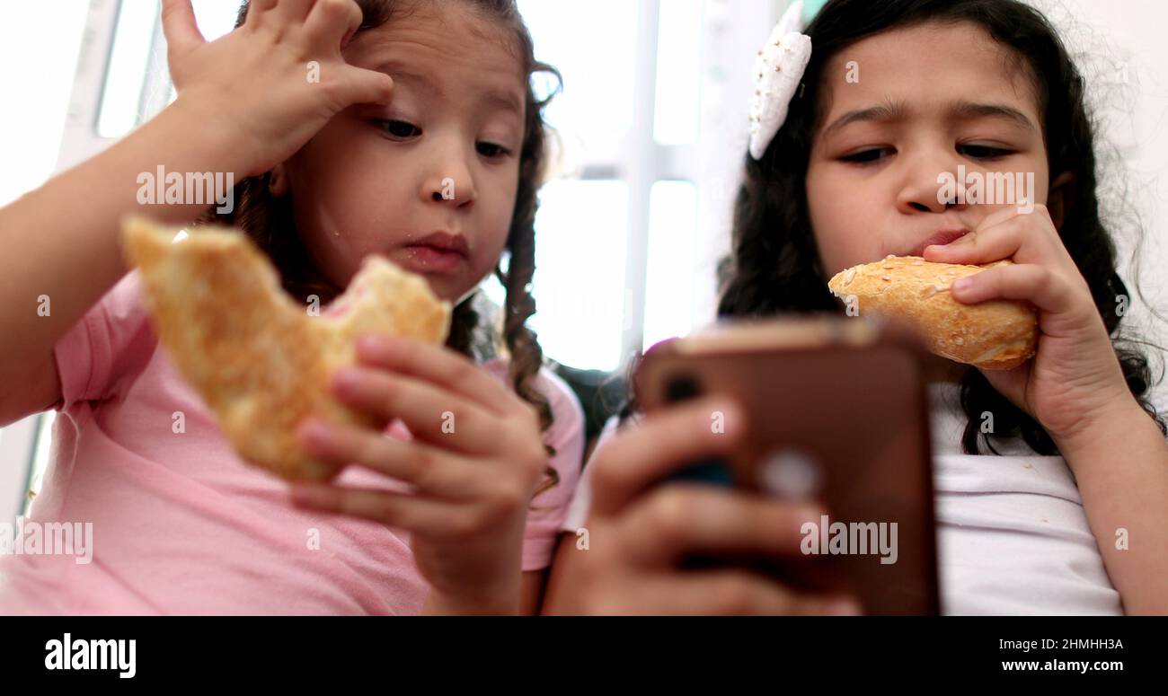 Generation Z little girls using mobile phone while eating sandwich ...