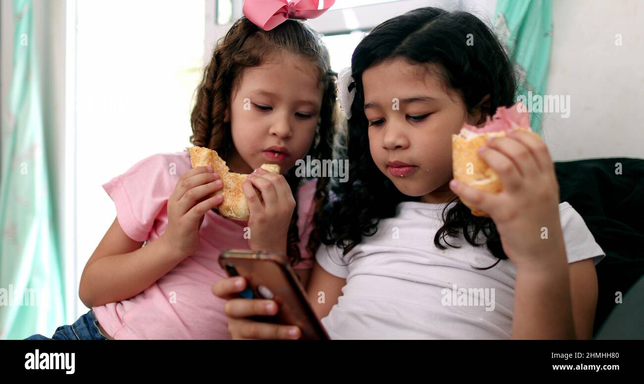Kids eating sandwiches while looking at smartphone, children snacking ...