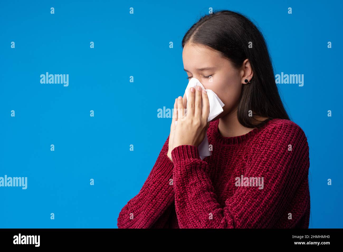 Teen girl blowing nose against blue background Stock Photo - Alamy