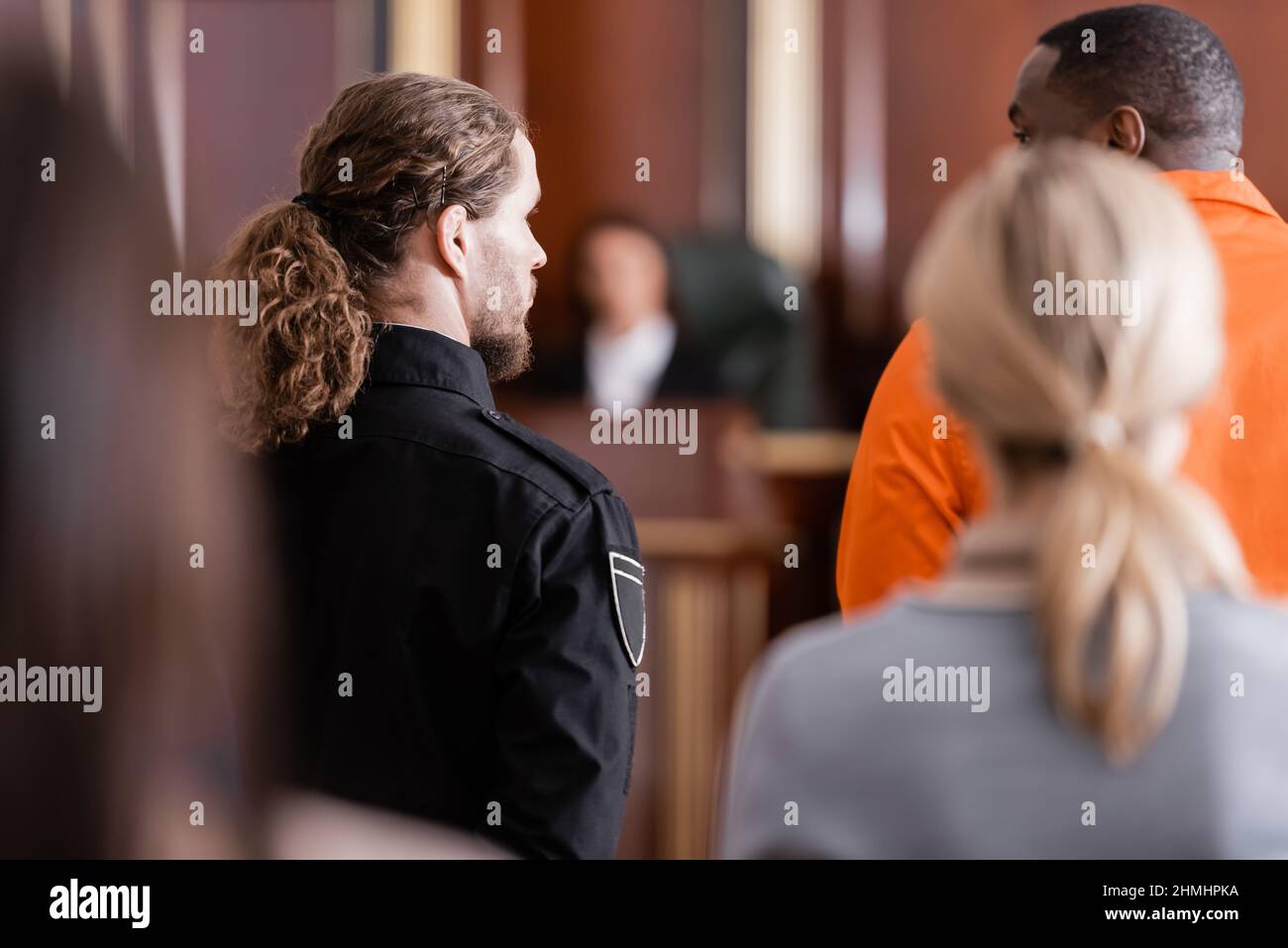 back view of accused african american man near guard and blurred jurors ...