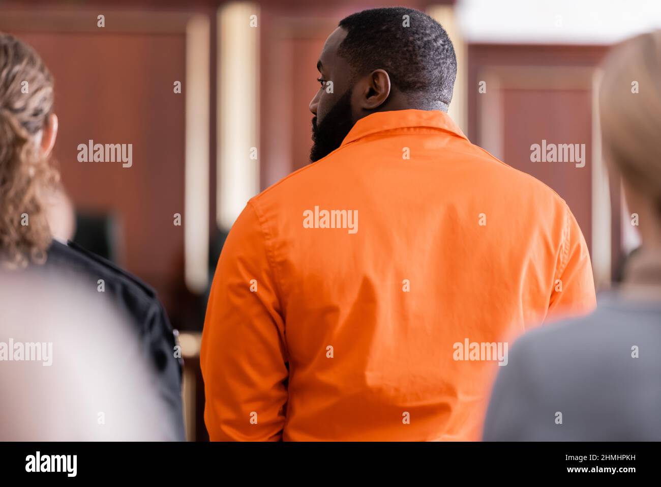 back view of african american man in jail uniform near guard and ...
