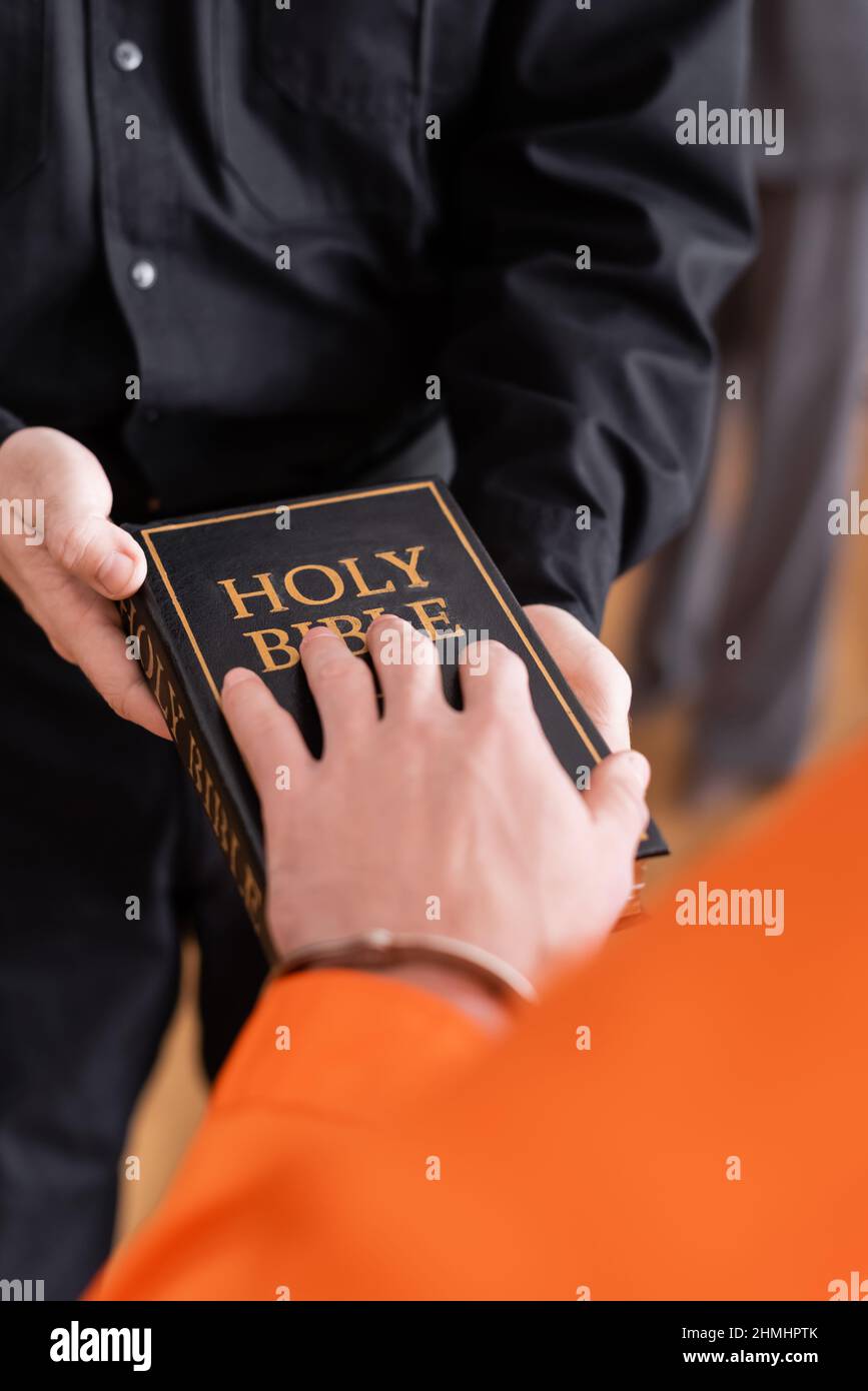 partial view of accused man giving oath on bible in court near bailiff ...