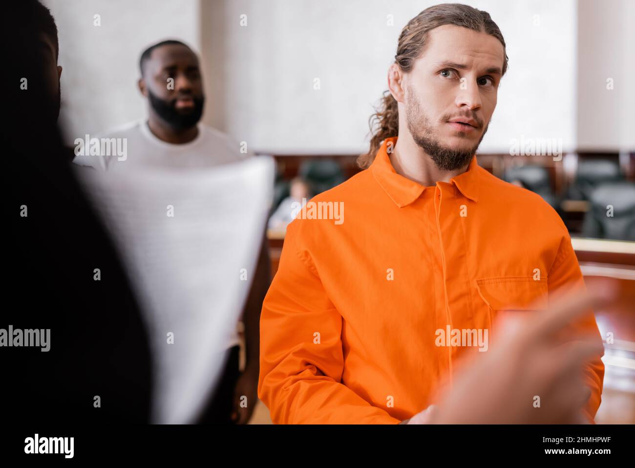 accused man in jail uniform looking at blurred prosecutor pointing with ...