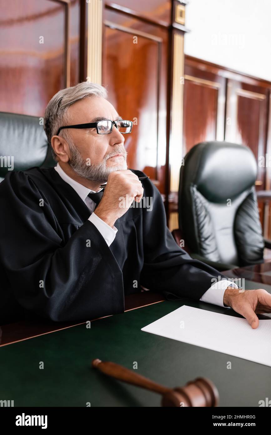 senior judge in robe and eyeglasses sitting with pen during litigation ...