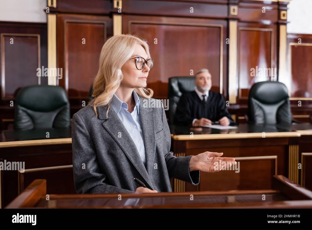 blonde advocate pointing with hand while talking in court near judge on ...
