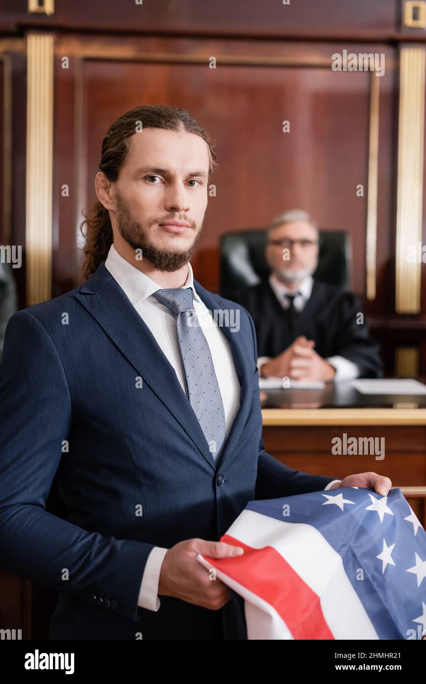 attorney looking at camera while holding usa flag near blurred judge in ...