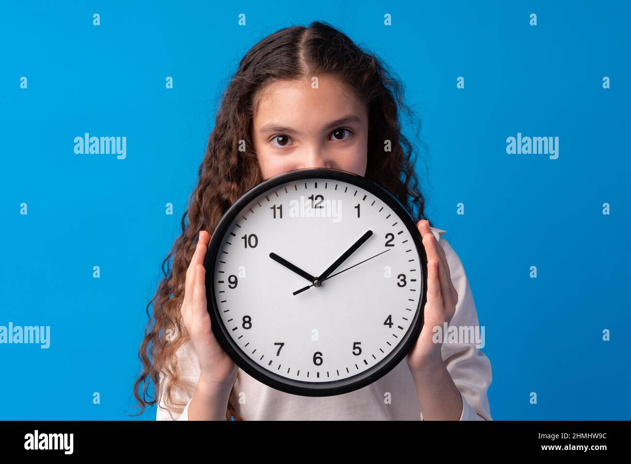 Beautiful teen girl holding wall clock over blue background Stock Photo ...