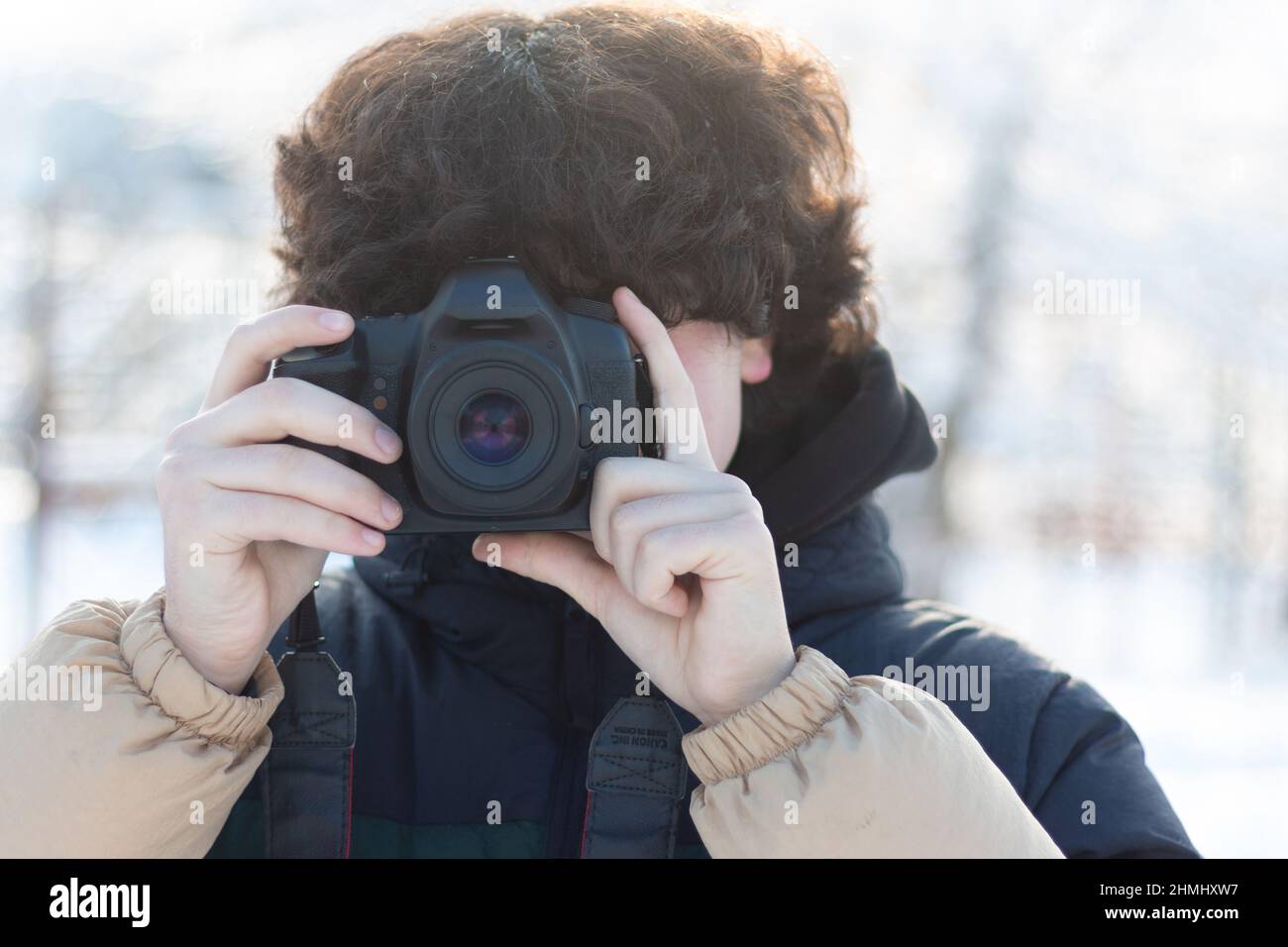 A teenage boy with curly long hair takes a picture with a digital SLR ...