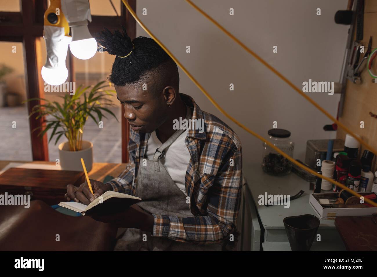 African american young craftsman writing on book while sitting in ...