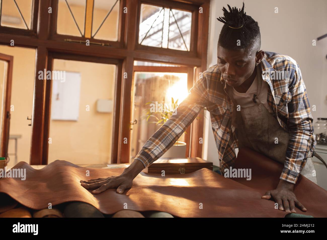 African american young craftsman analyzing leather on workbench in ...