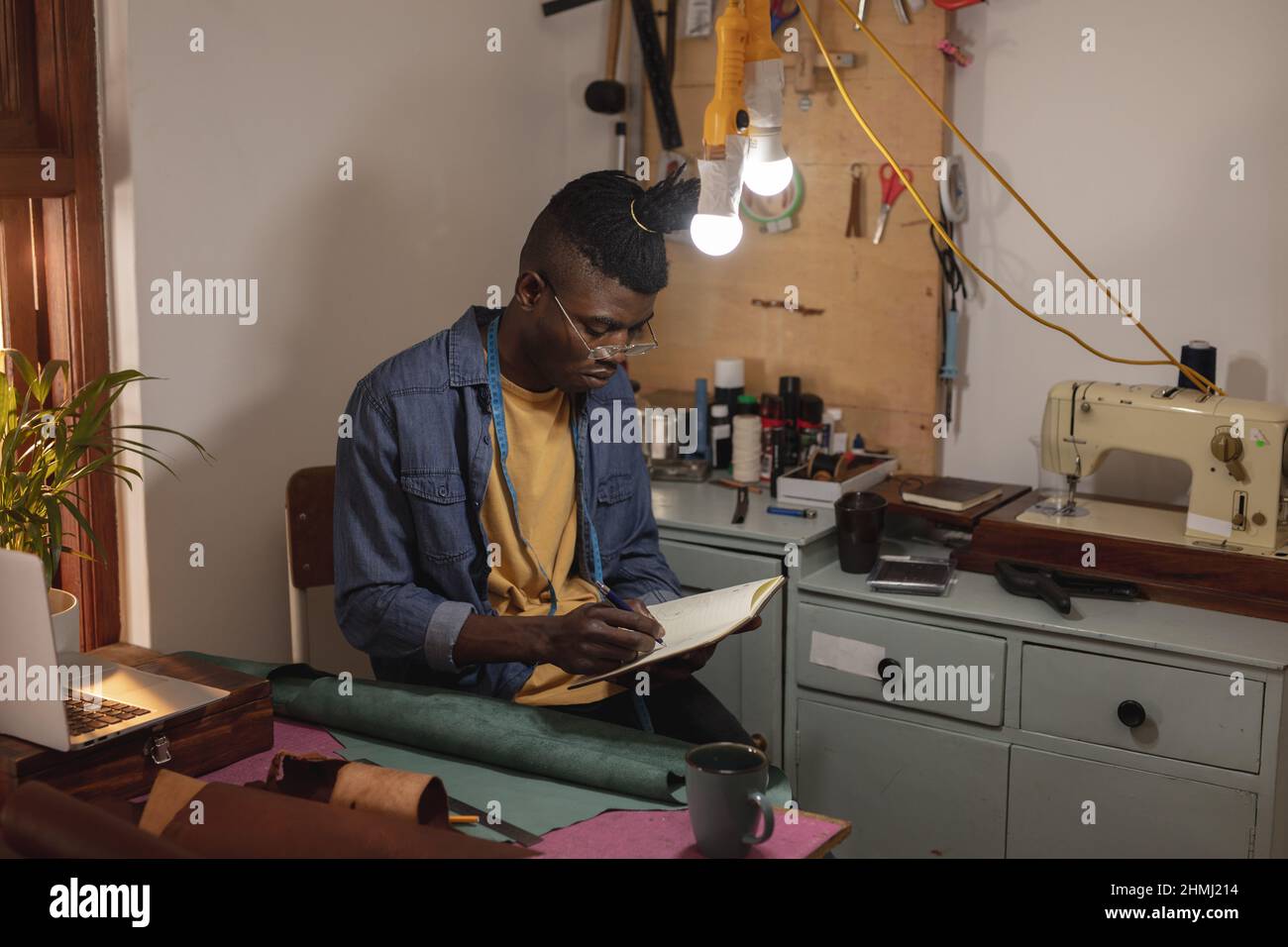 African american young craftsman writing on book while sitting with ...