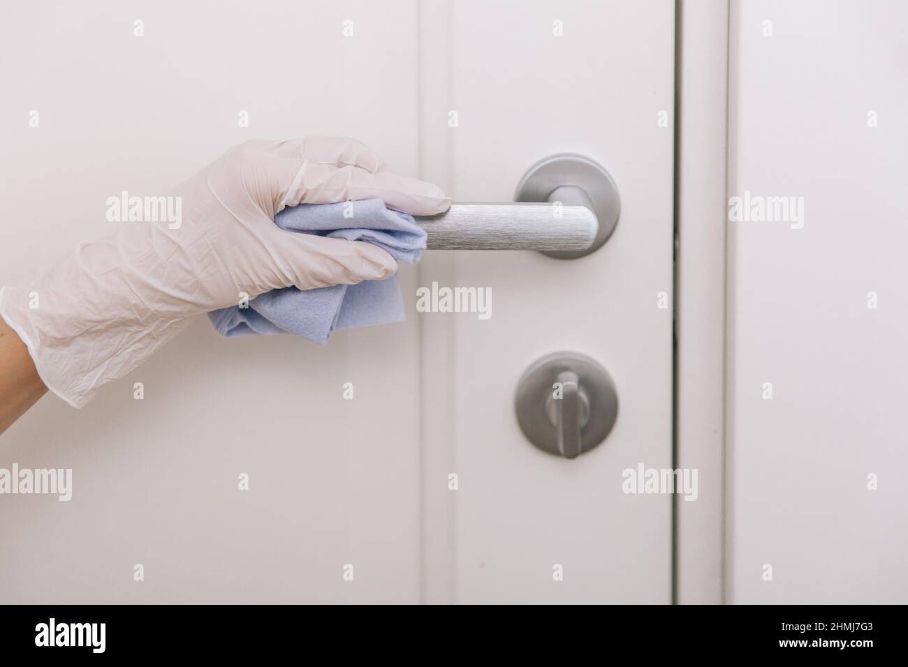 Cleaning door handle with blue wipe in white gloves. Woman hand using ...