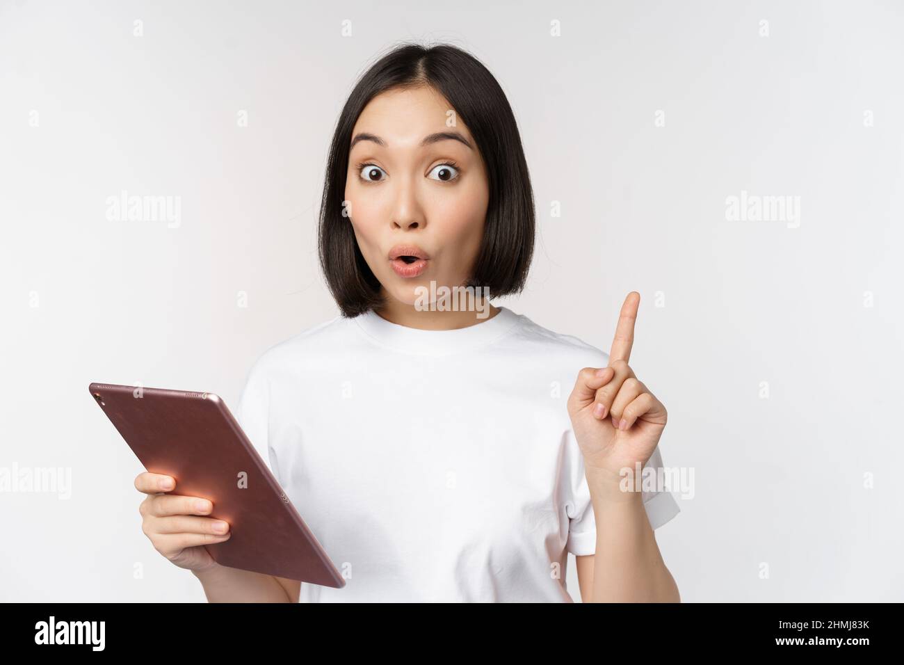 Enthusiastic asian woman with tablet, raising finger and looking amazed ...