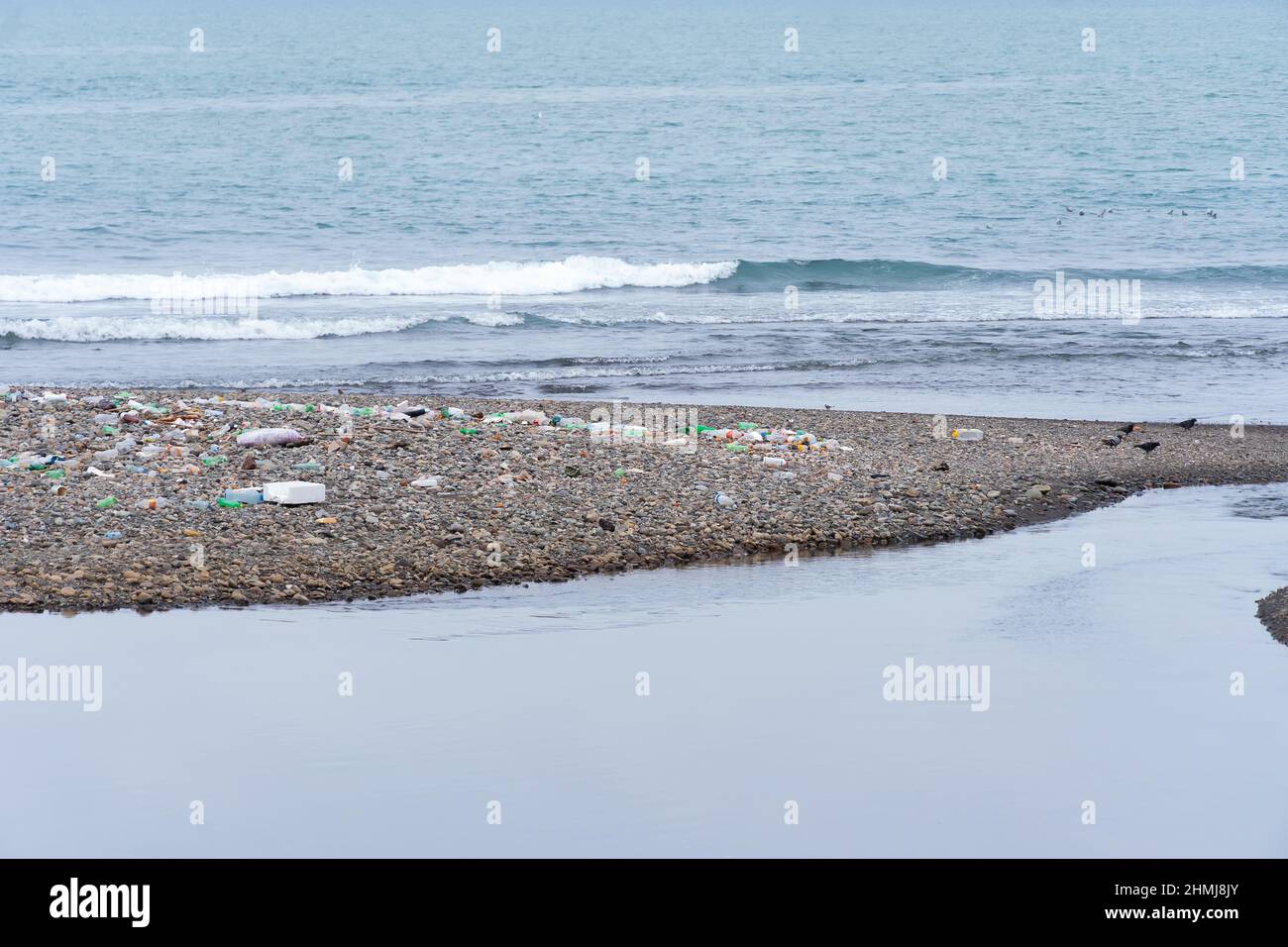 Bottles, plastic, garbage on the pebble beach of the sea. River flows ...