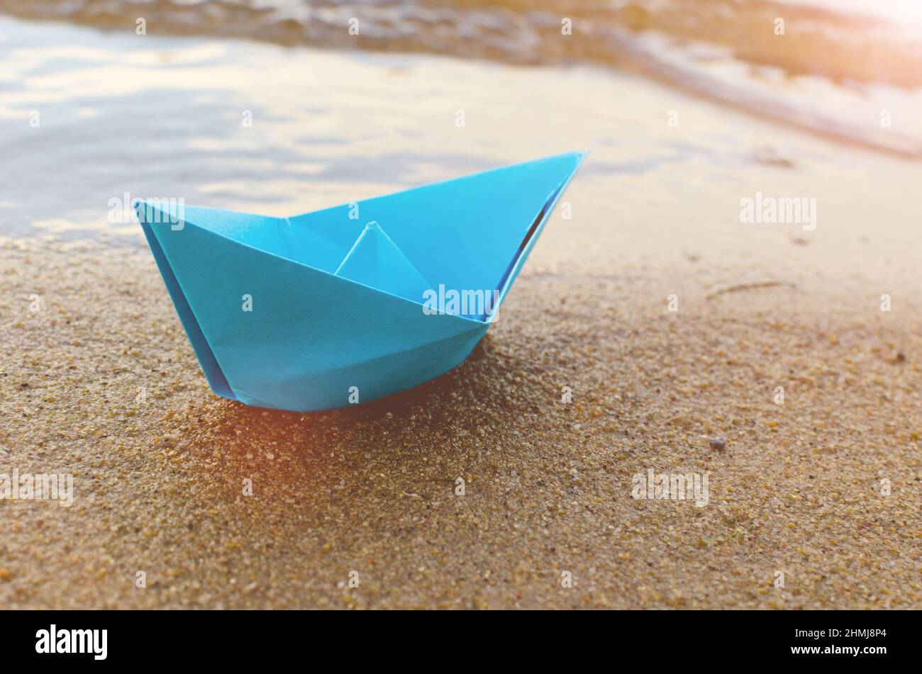 Blue paper boat in the sand on the ocean, early in the morning in the ...