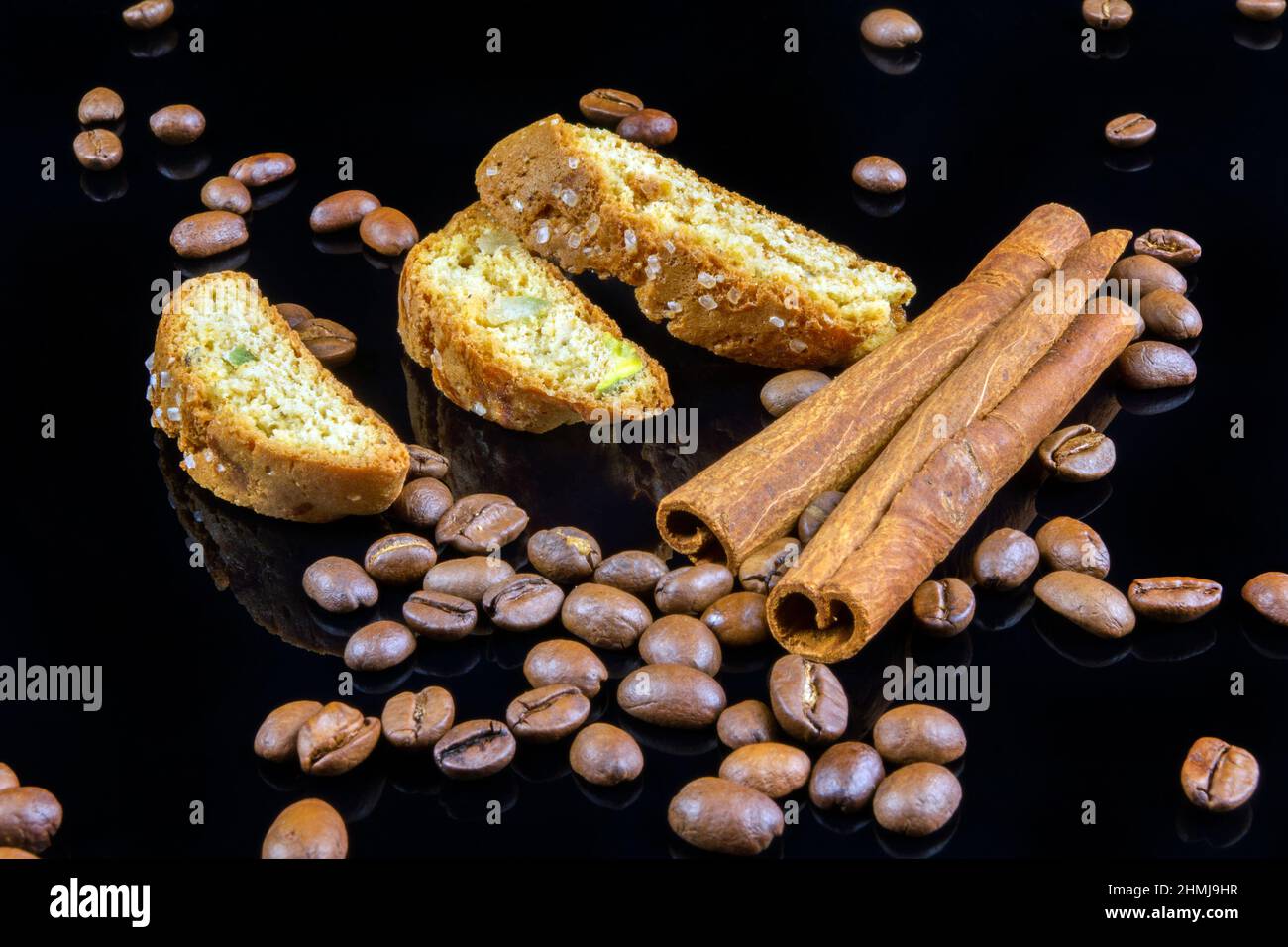 A coffee beans, bisquits and cinnamon sticks over black reflective ...