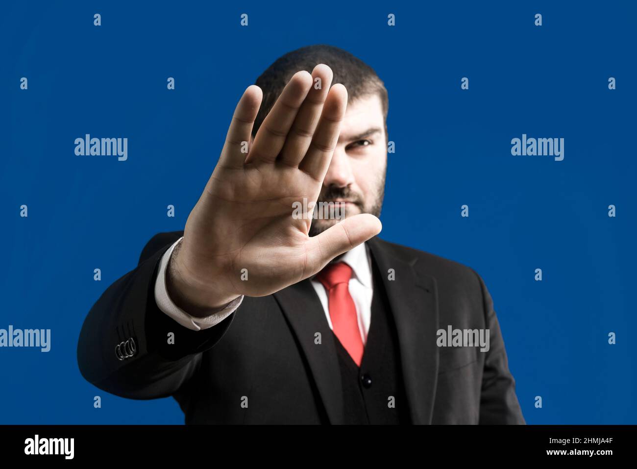 A man in a suit holds out his palm in front of a blue background. Stop ...