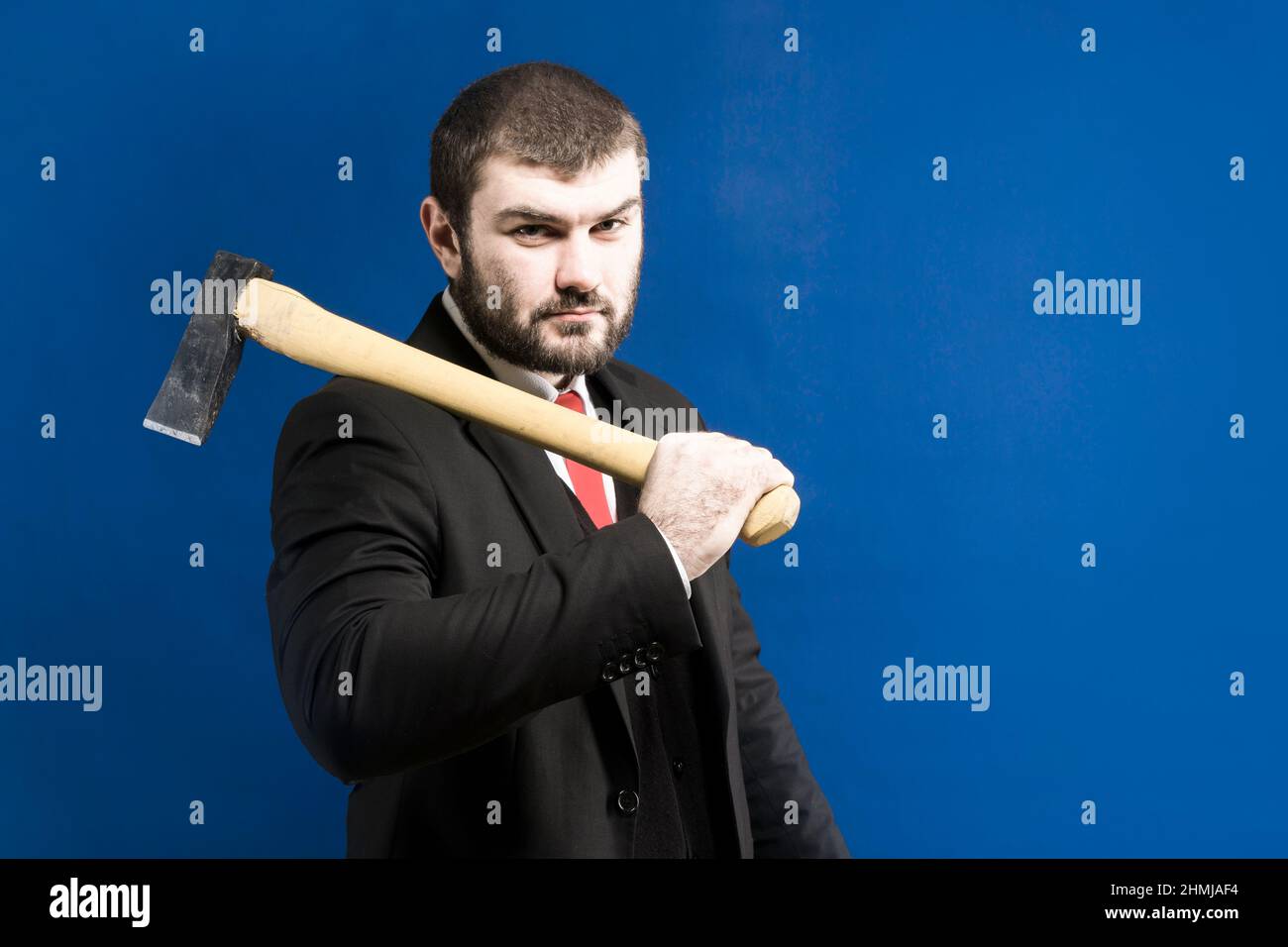 A man with a beard in a suit and a red tie holds an ax on his shoulder ...