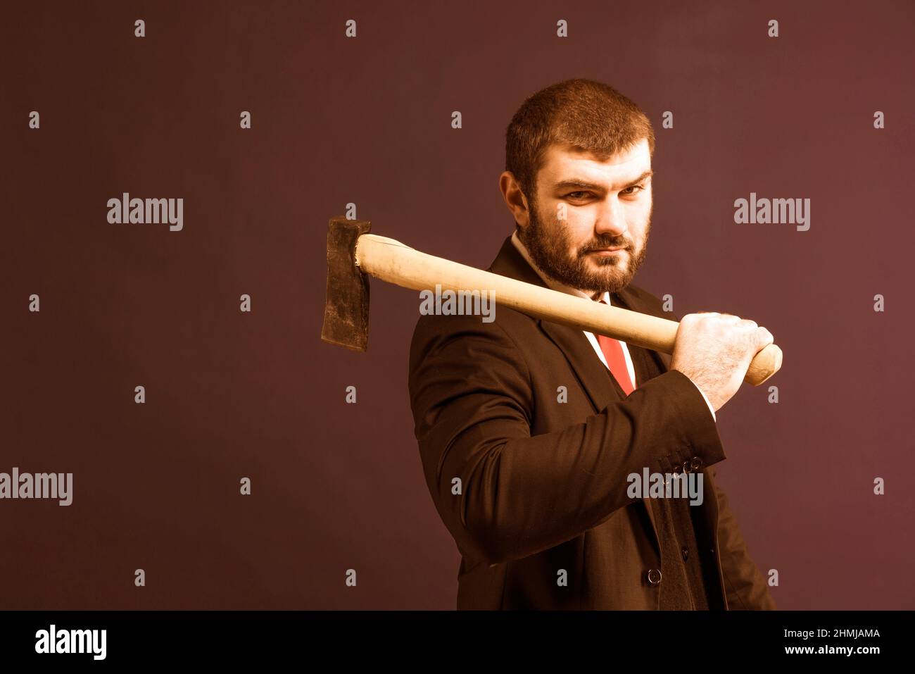 A man with a beard in a suit and a red tie holds an ax on his shoulder ...