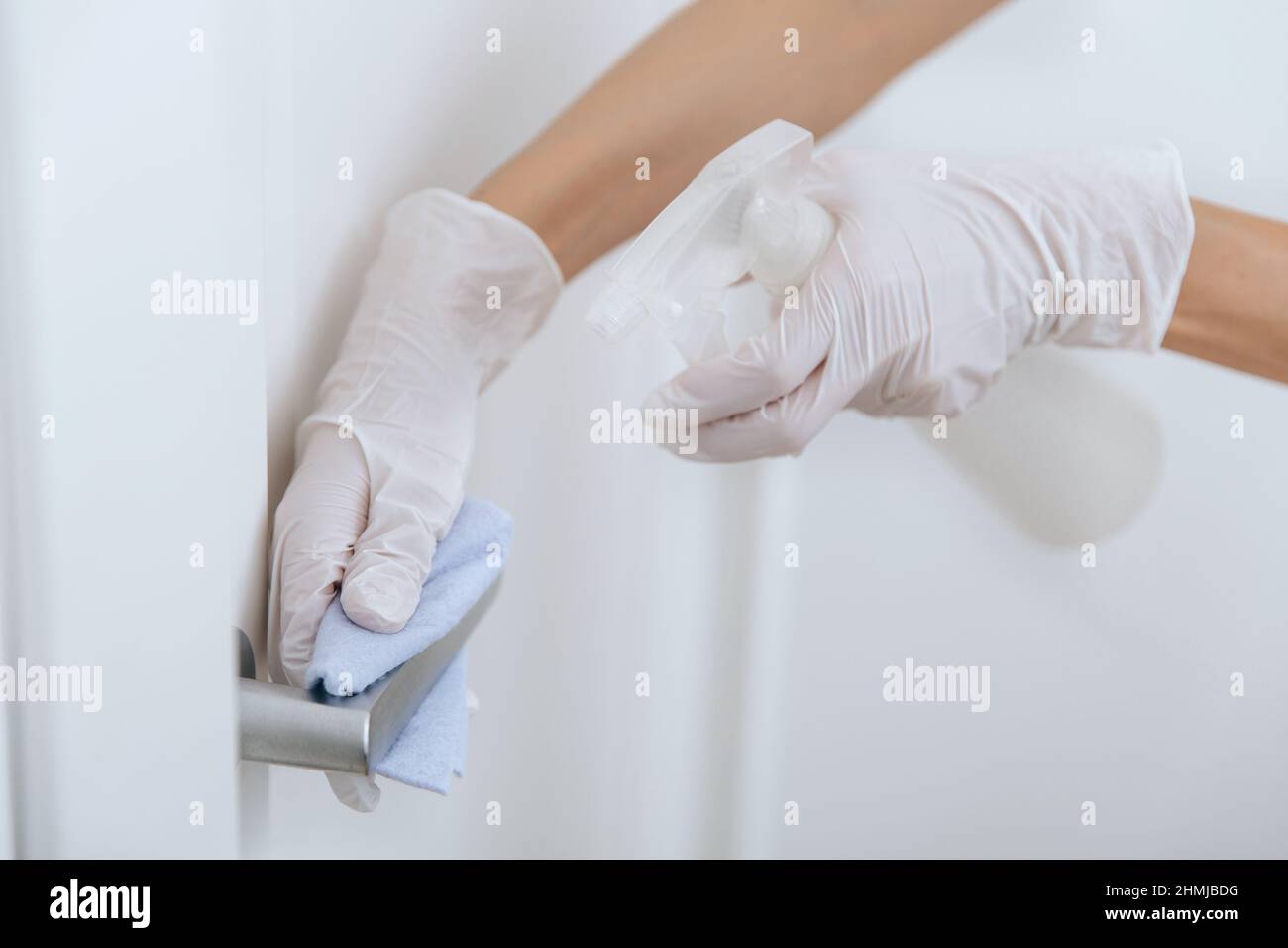 Cleaning door handle with blue wipe in white gloves and sanitizer spray ...