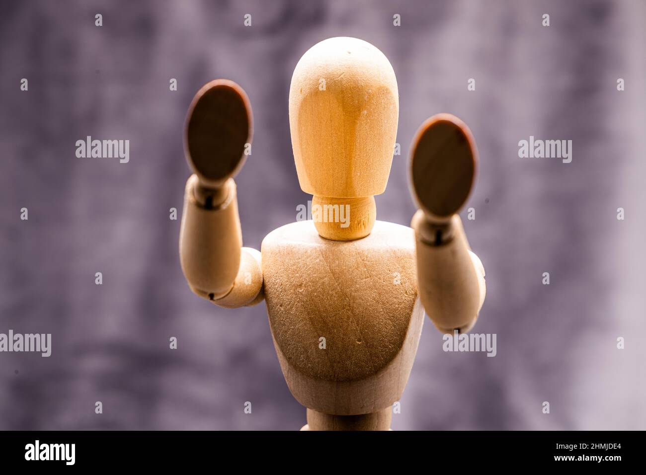 Closeup shot of a small wooden human mannequin with hands up against a ...