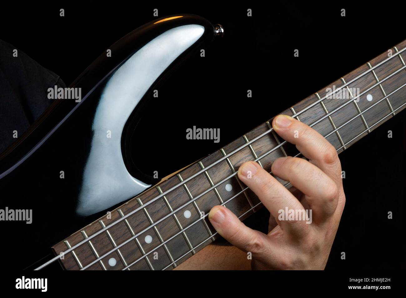 Guitarists hand playing on the fretboard of an electric bass guitar ...