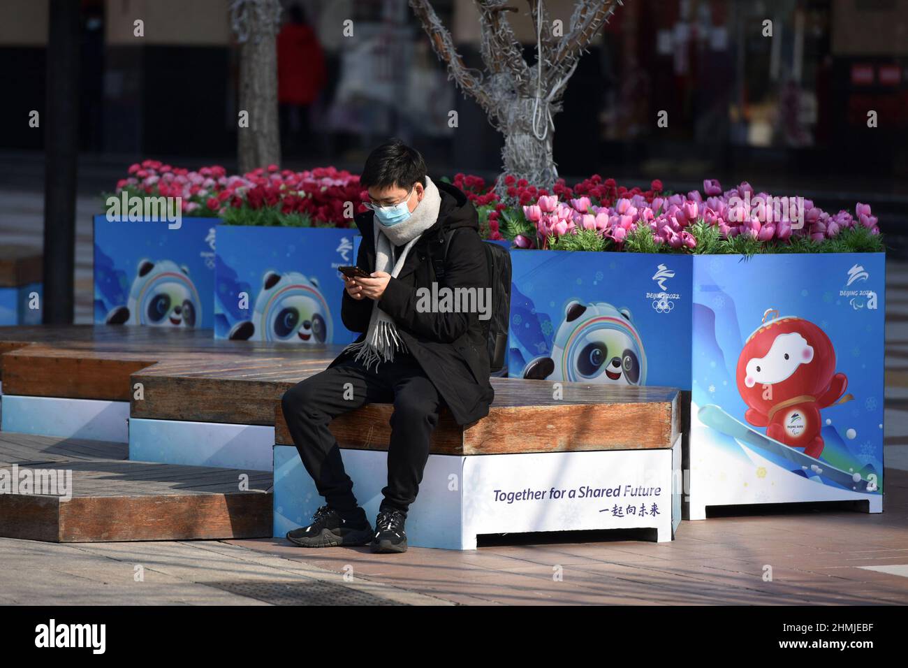 Beijing, China. 10th Feb, 2022. A man sits near posters of "Bing Dwen Dwen" and "Shuey Rhon Rhon ...