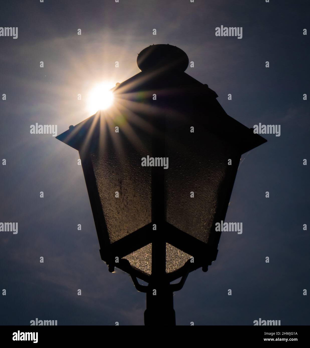 A street lantern,with the sun peaking up behind it, backlighting the ...