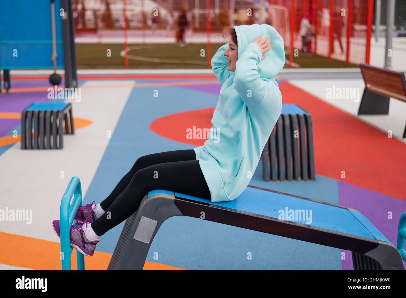 Caucasian woman in mint sweatshirt doing abdominal exercises outdoors ...