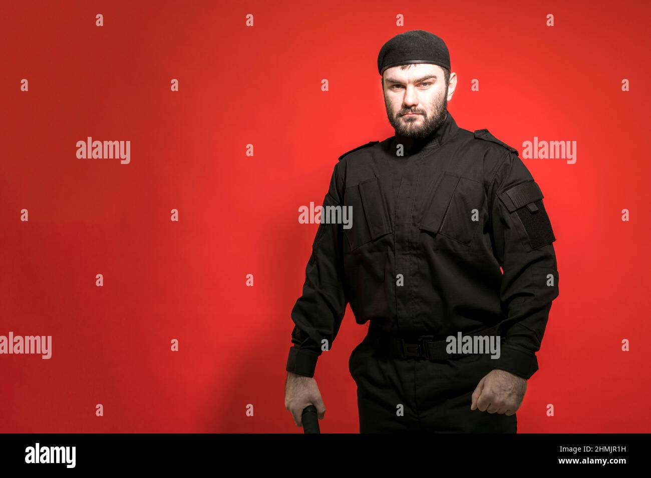 A male security guard in a black uniform and a cap on a red background ...