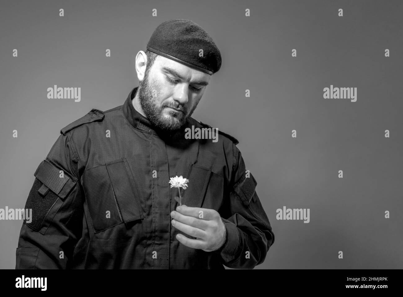 A male guard in a black uniform and a cap holds a flower in his hand ...