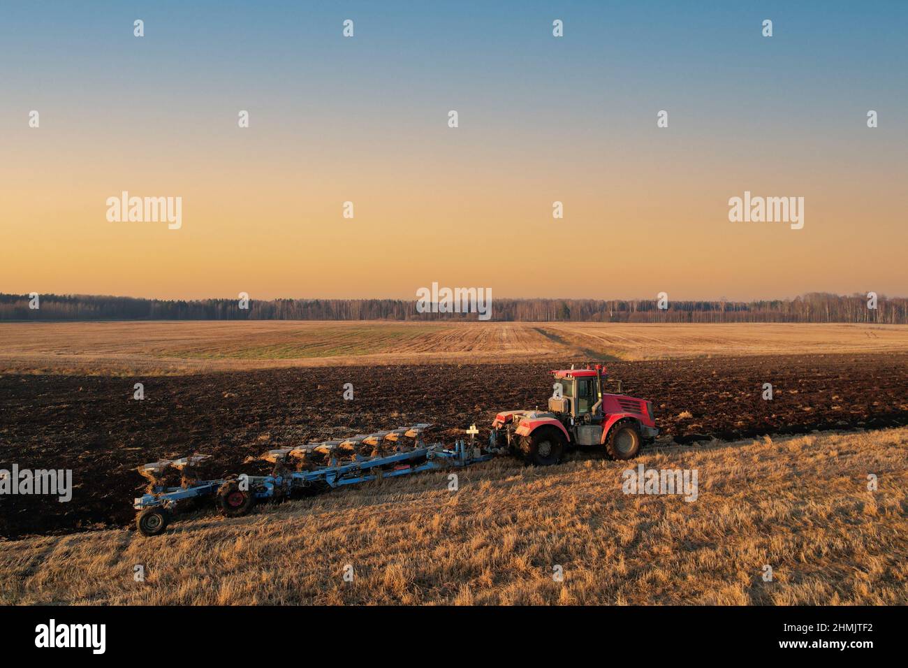 Tractor Plowing field on sunset. Red Tractor with Plough on Plowed ...