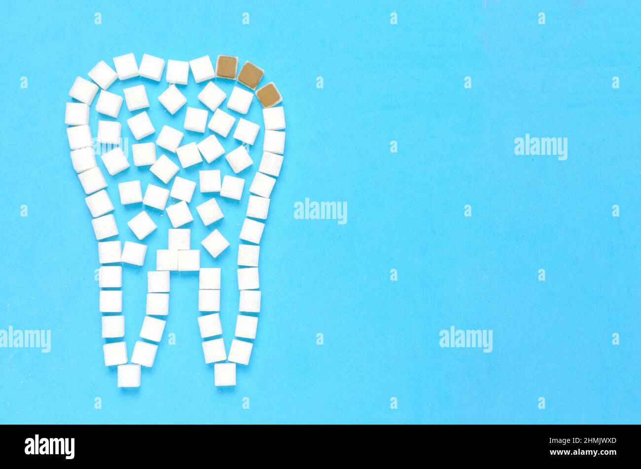 Refined sugar in form of tooth with caries on blue background.The ...