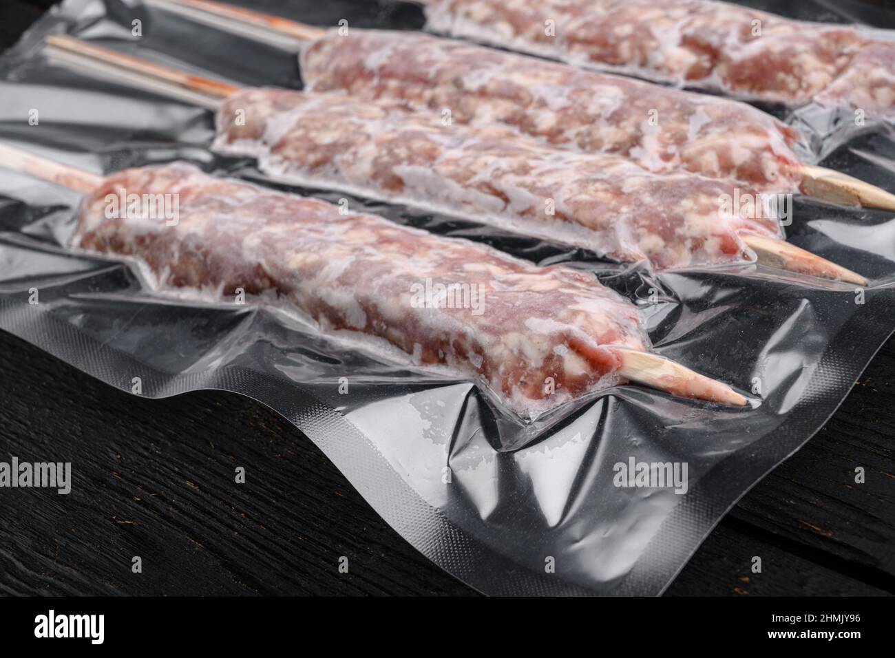 Mutton minced meat on skewers in vacuum pack set, on black wooden table ...