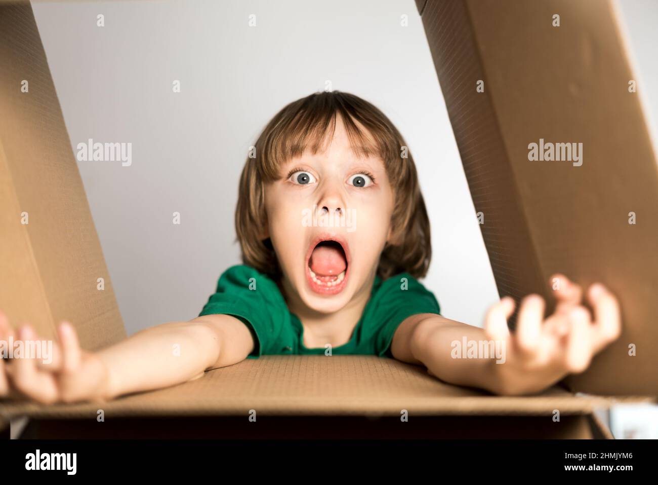 Funny little boy jumping with scary face jumping out of the cardboard ...