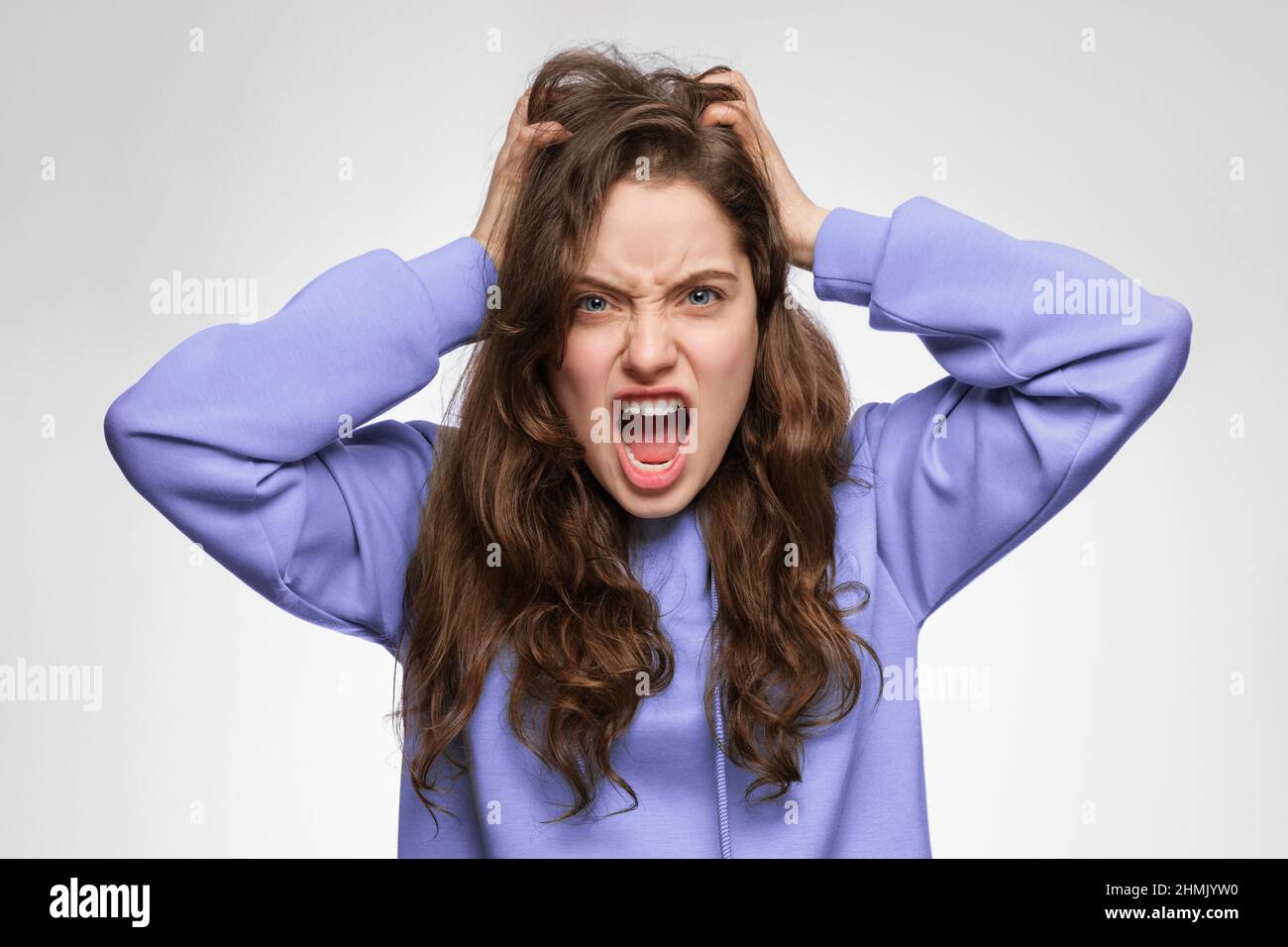 The young woman is angry and screaming, holding her head. Girl with ...