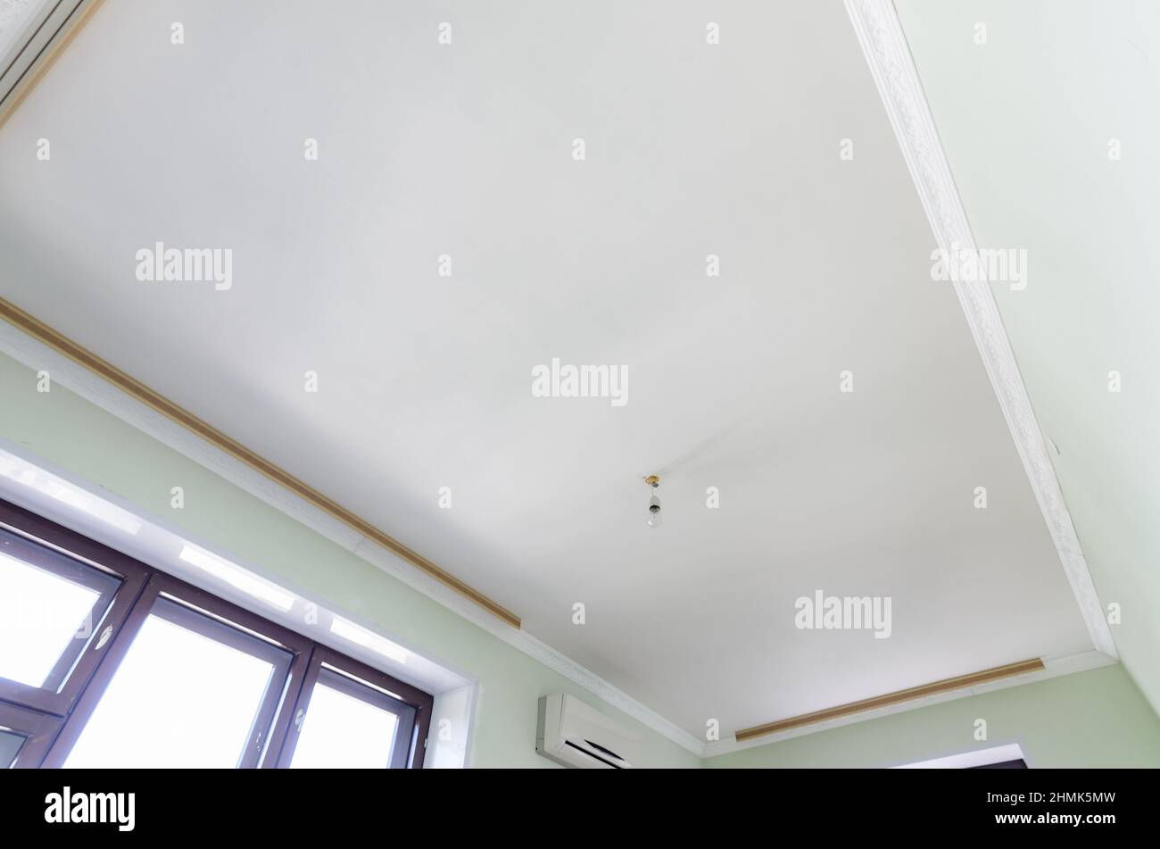Plastered white ceiling in the room, a temporary light bulb hangs on ...