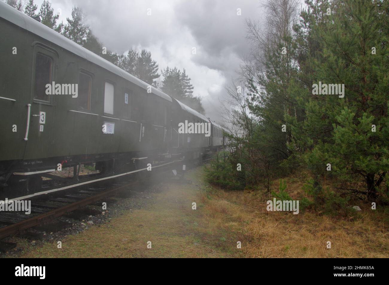 An old green passenger railroad car pulled by a steam engine leaving ...