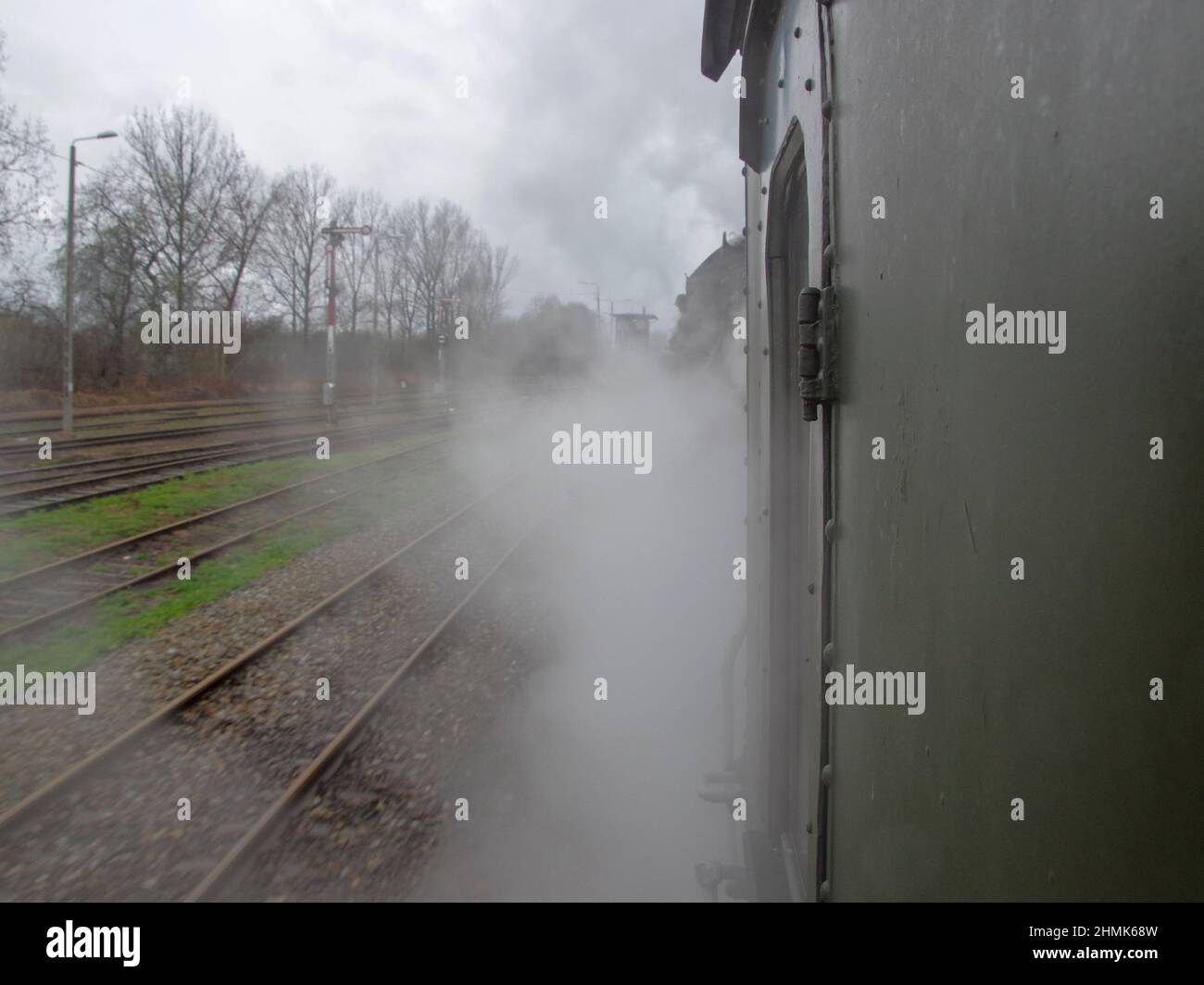 An old green passenger railroad car pulled by a steam engine leaving ...