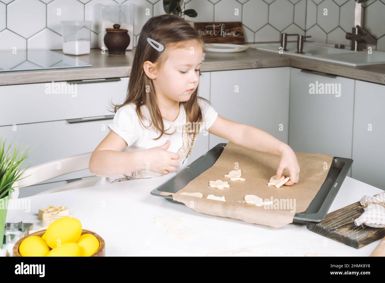 Portrait of little studiously girl chef, sitting on chair, making ...
