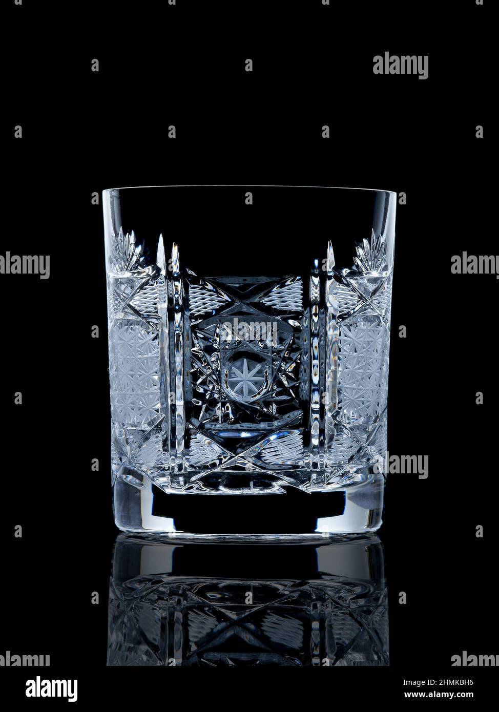 Empty crystal whiskey glass on black reflective surface with rim light ...