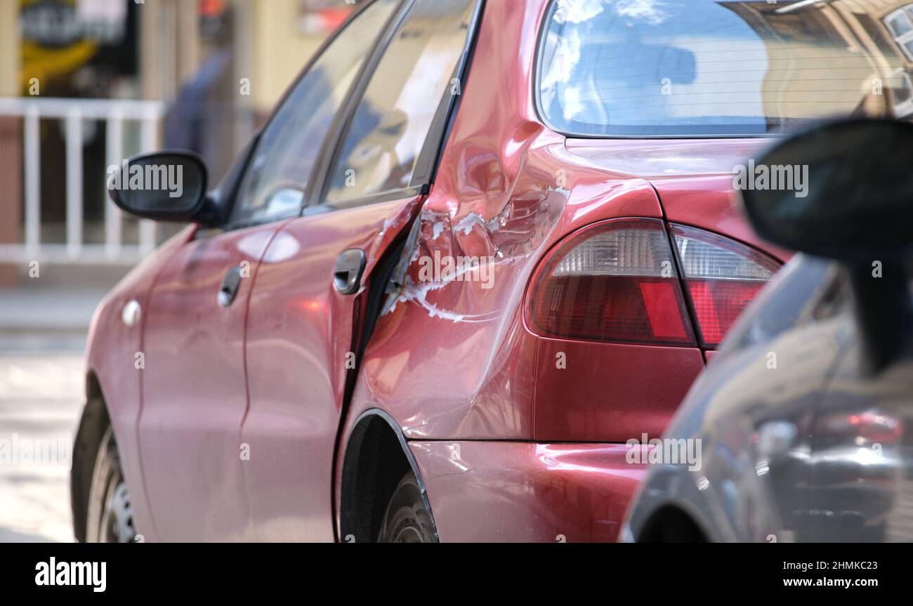 Dented car with damaged body parked on city street side. Road safety ...
